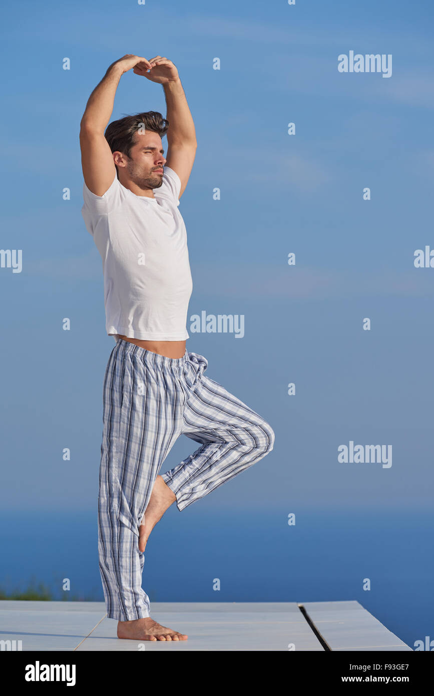 handsome young man practicing yoga on in modern home terace with ocean ...