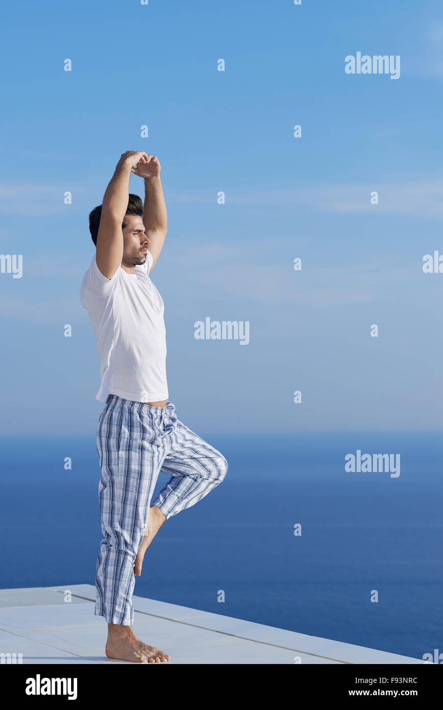 handsome young man practicing yoga on in modern home terace with ocean ...