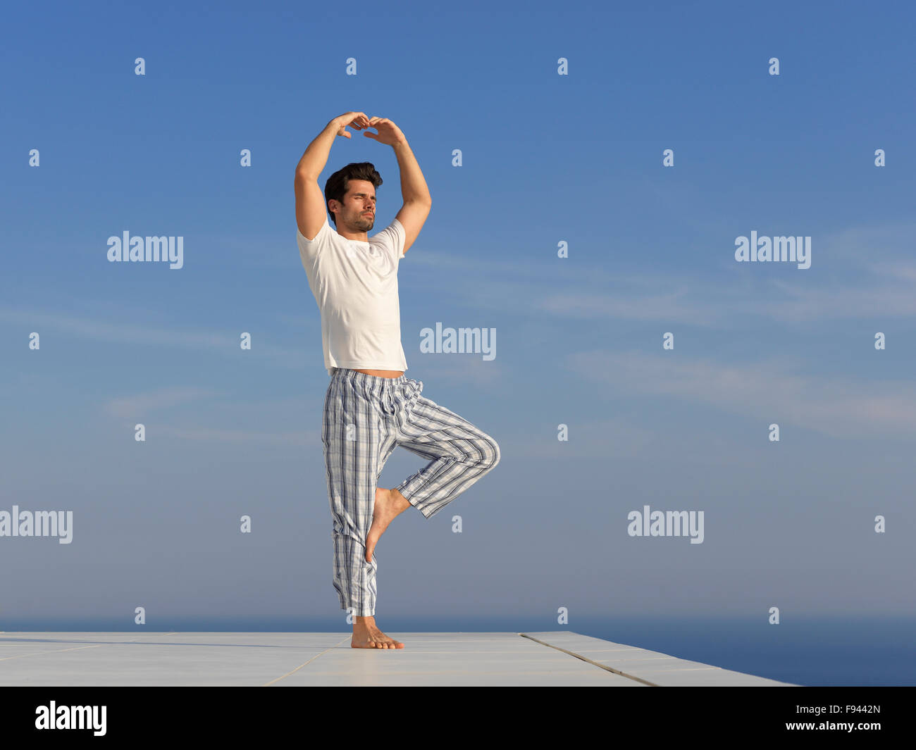 handsome young man practicing yoga on in modern home terace with ocean ...