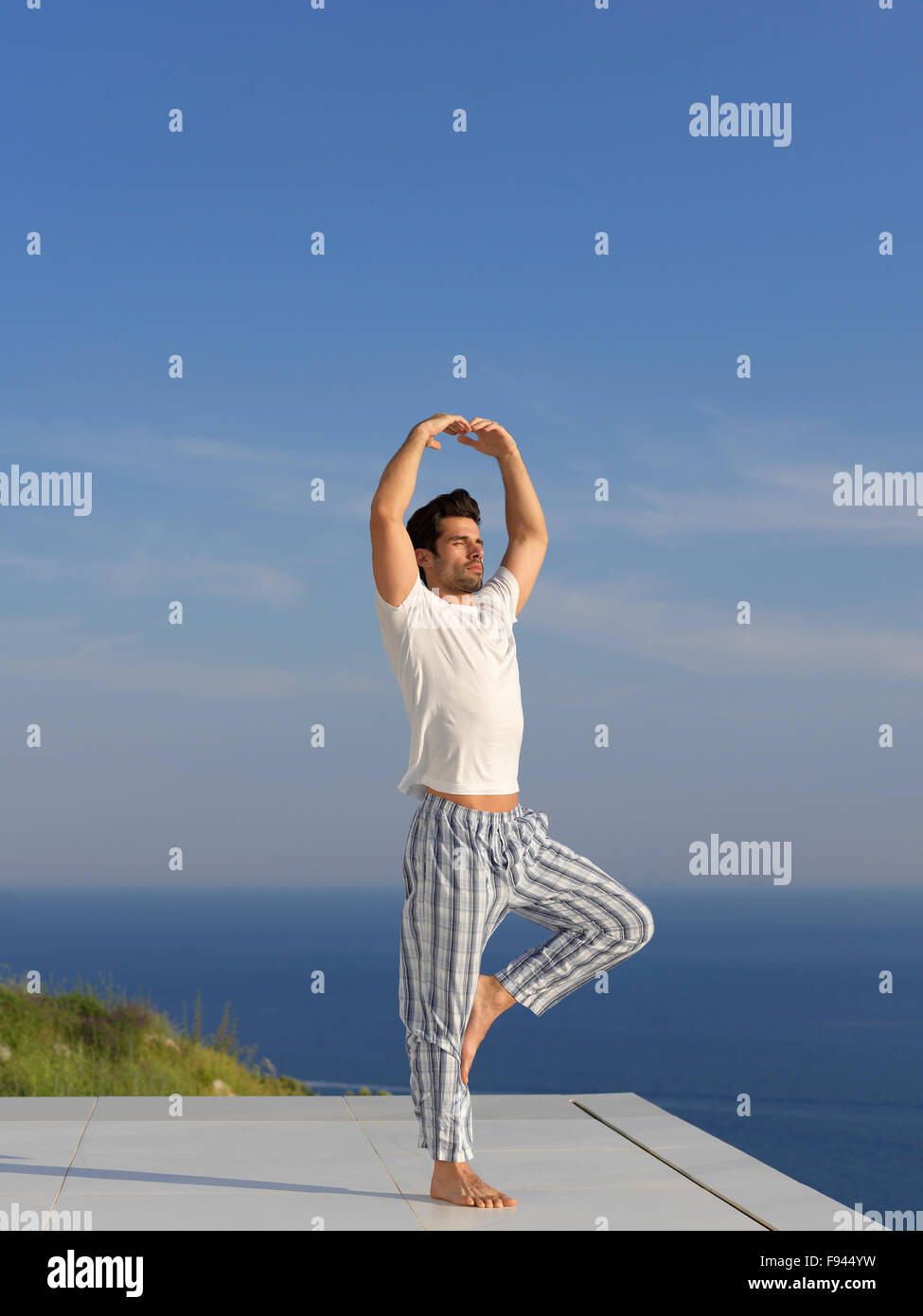 handsome young man practicing yoga on in modern home terace with ocean ...