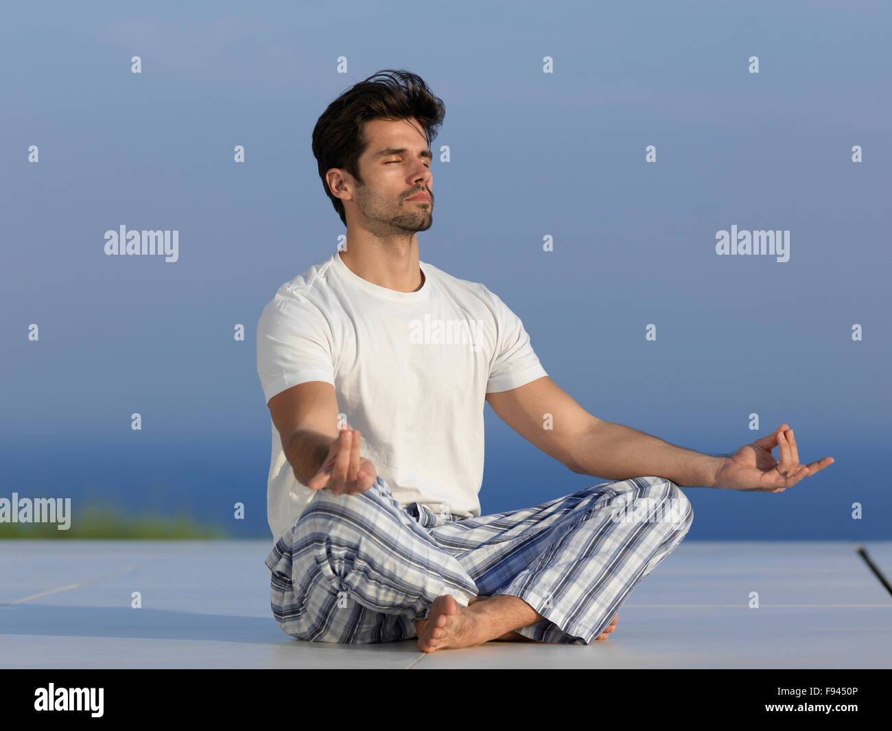 handsome young man practicing yoga on in modern home terace with ocean ...