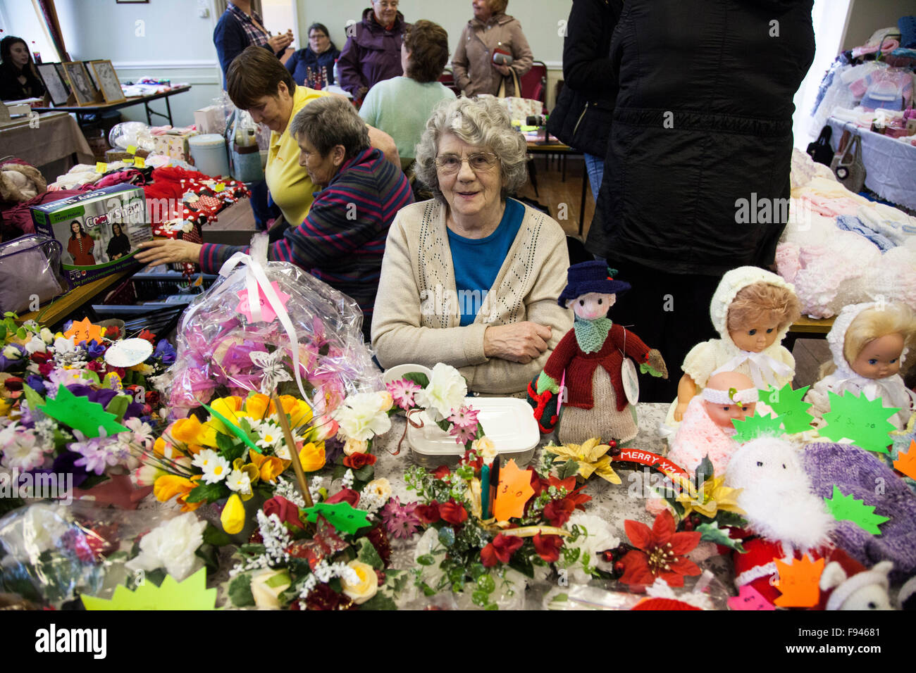 An elderly woman sits in a craft fair with her knitted goods Stock ...