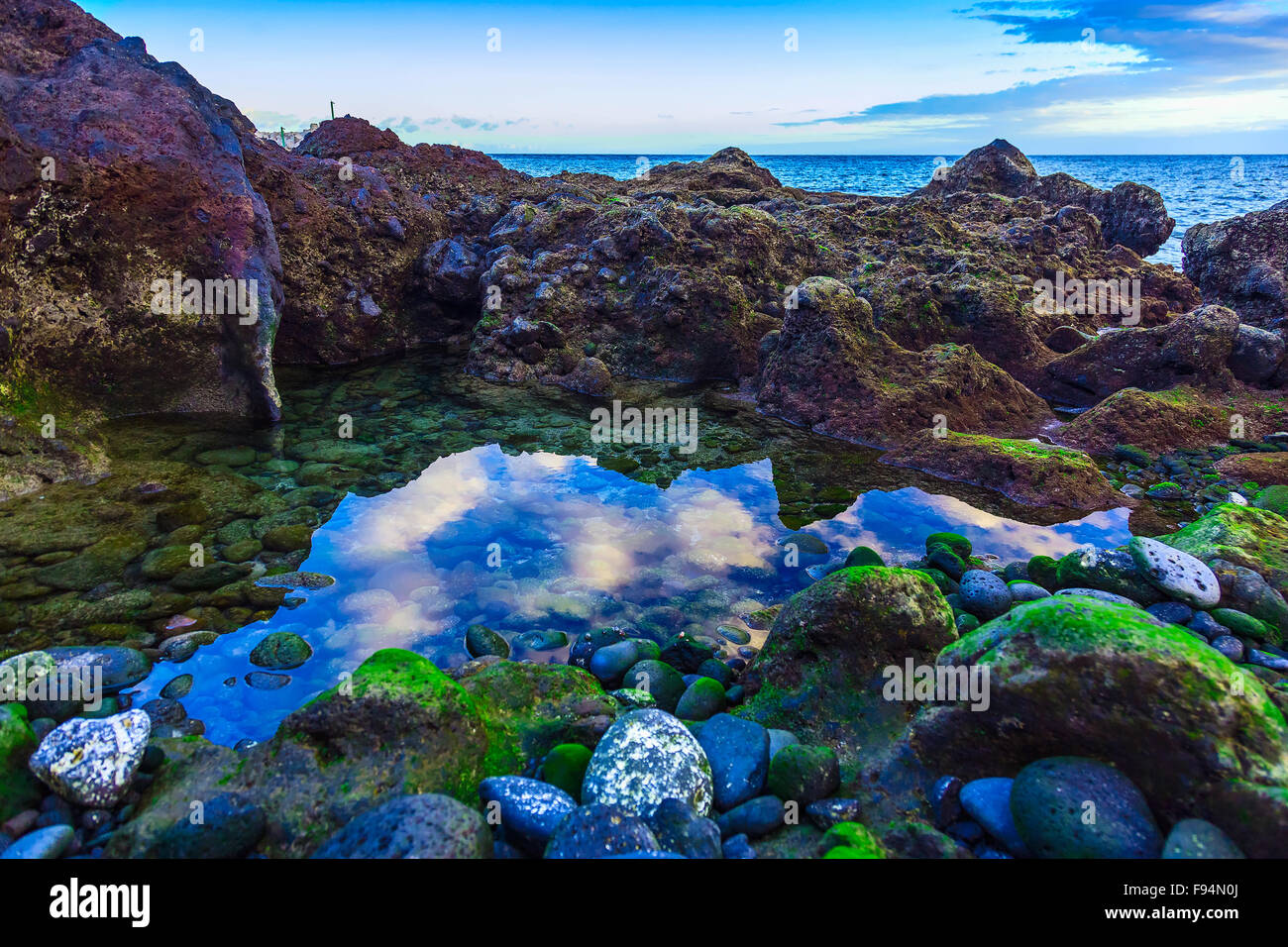 Stone Shore of Ocean with Sky Reflection in water on Tenerife Island in ...