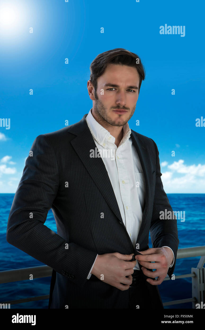 Young handsome man leaning against handrail on cruise ship, wearing ...