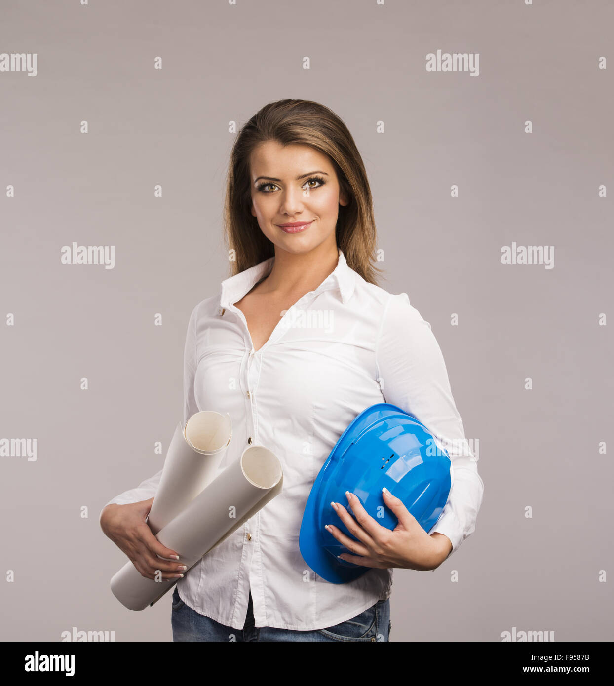Portrait of Young woman architect with blue hard hat and paper plans ...
