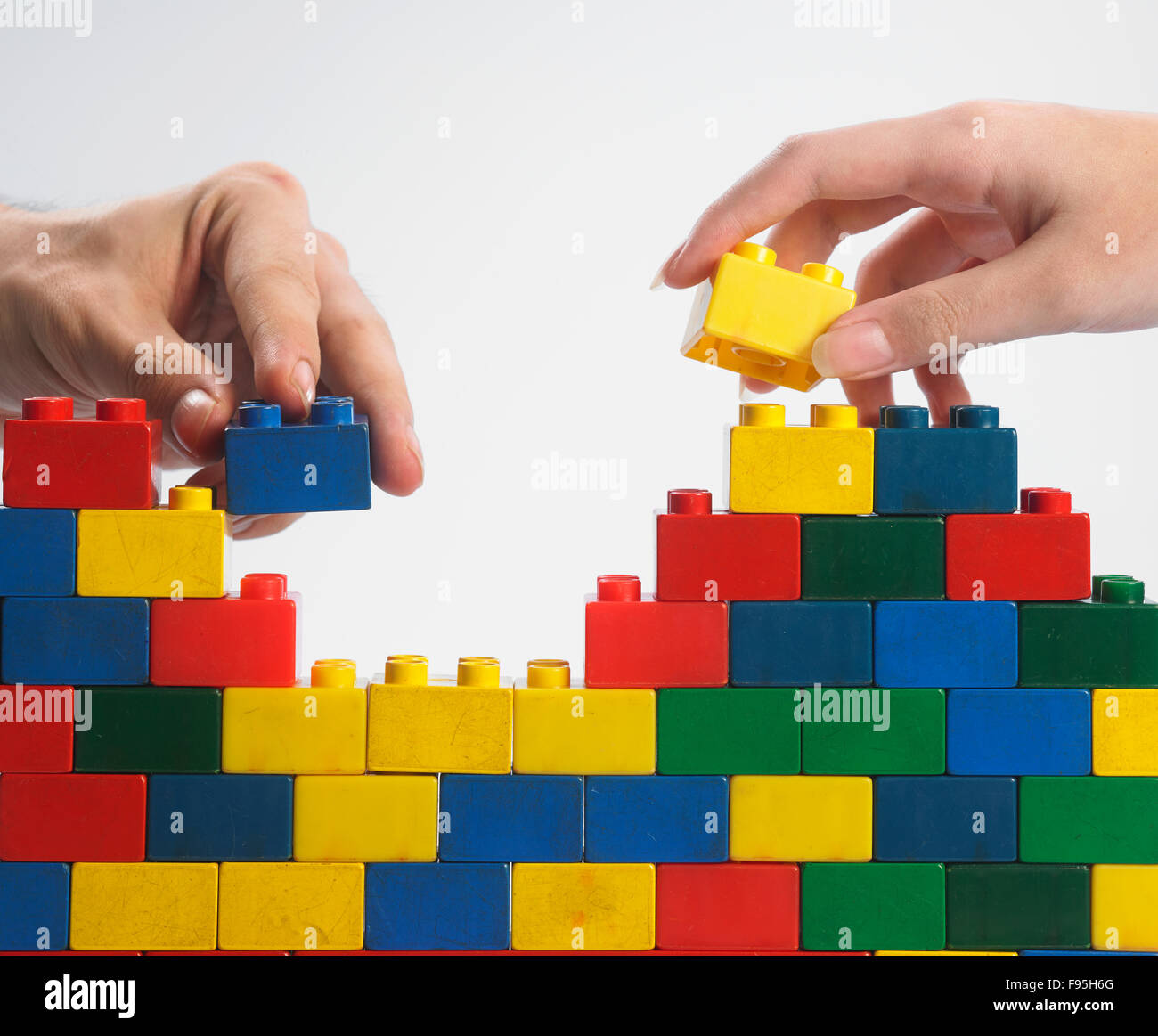 two hands teamwork stack up lego set as a wall on white background ...