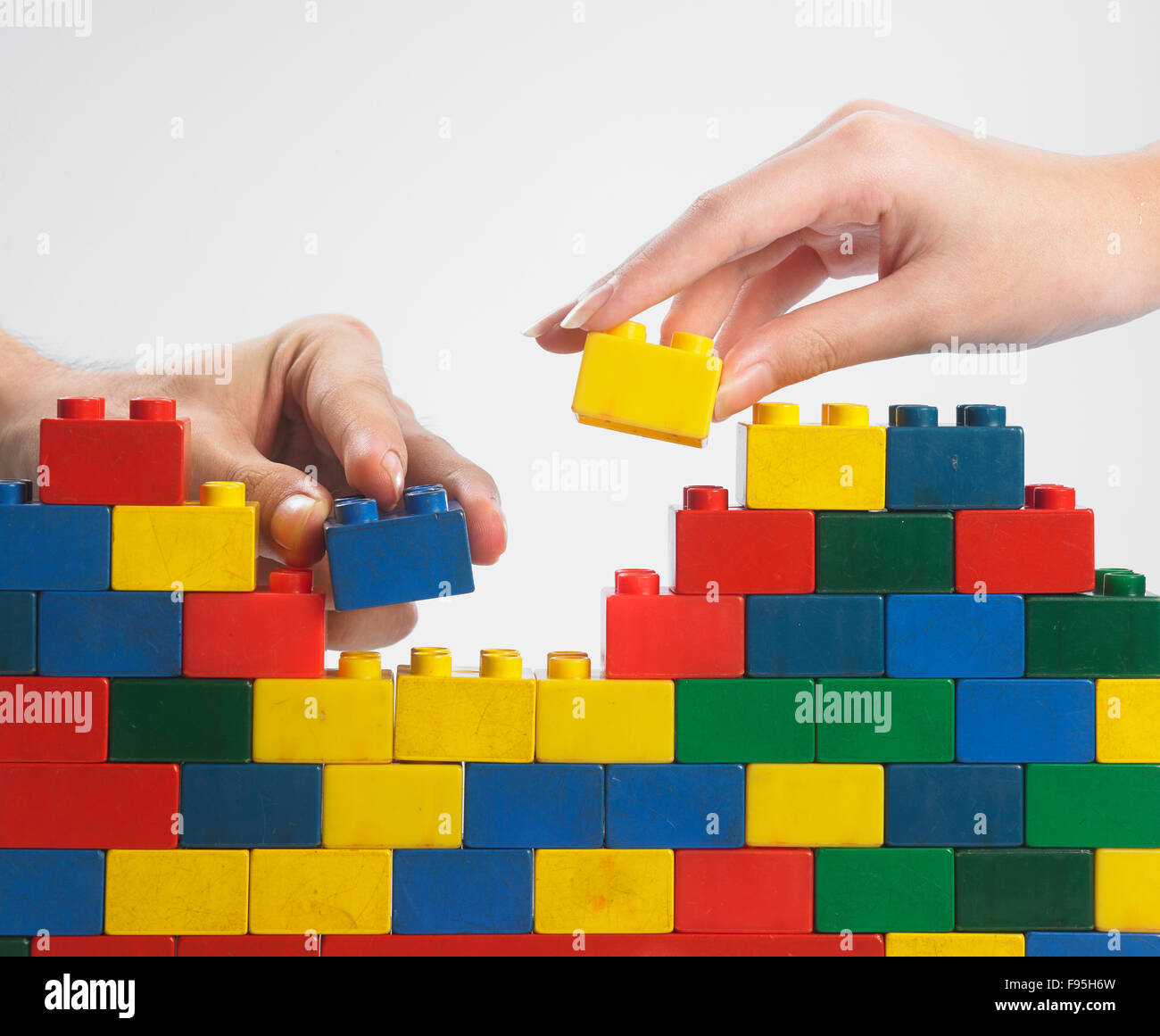 two hands teamwork stack up lego set as a wall on white background ...