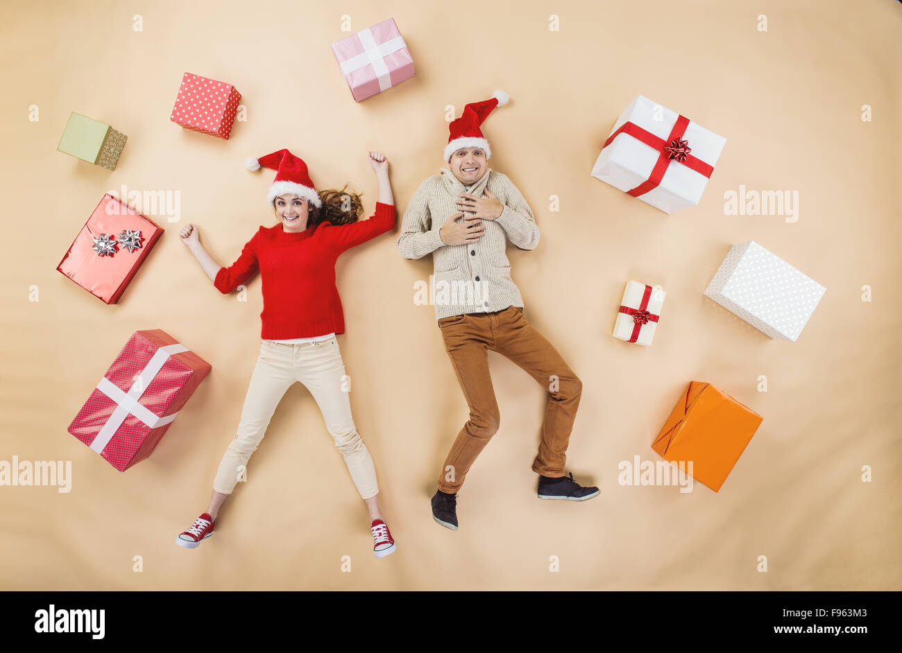 Happy young couple with Christmas presents jumping against the beige ...
