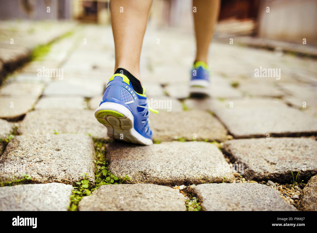 Female runner running on tiled pavement in city center, closeup on ...