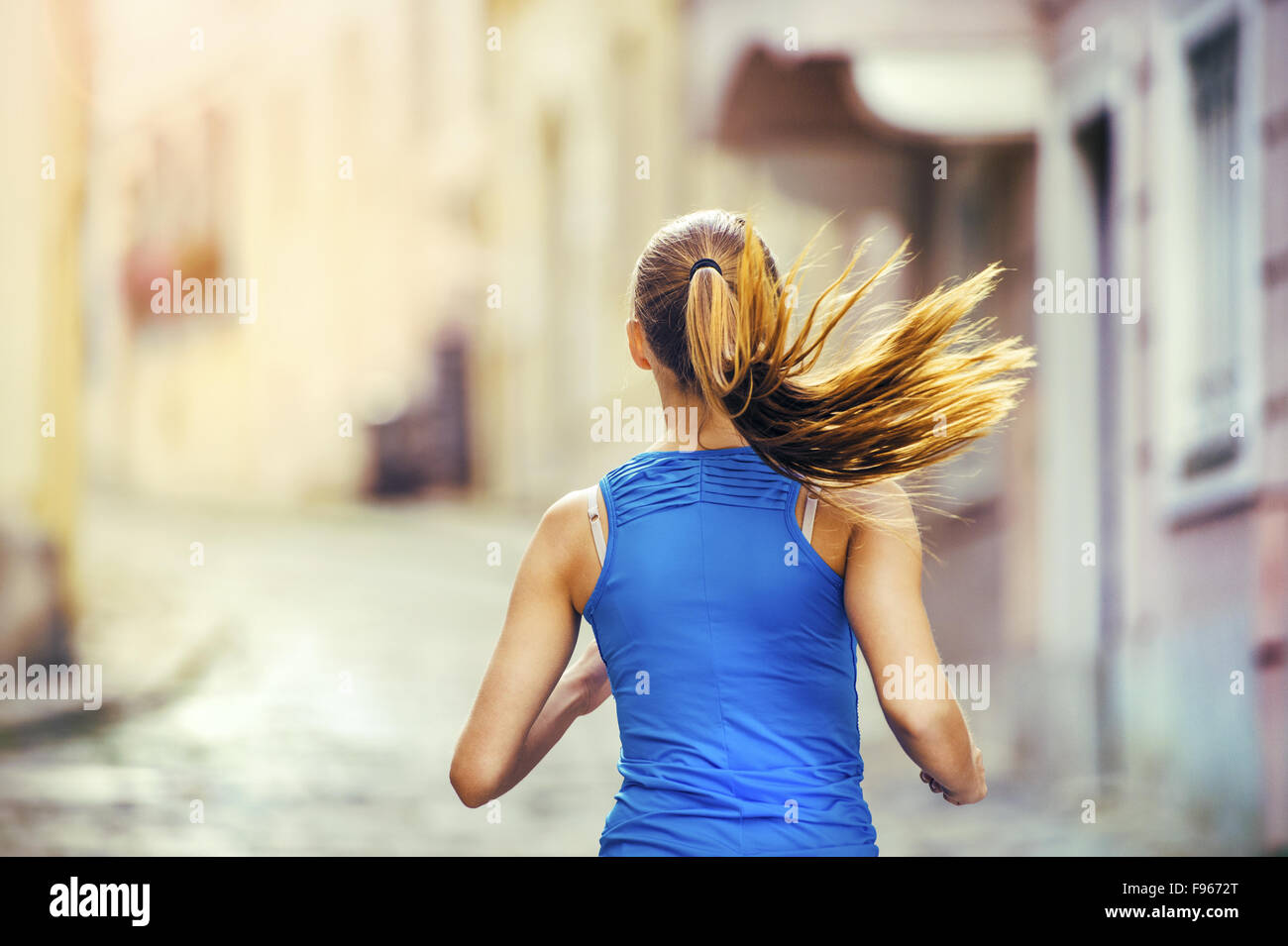Young female runner is jogging on tiled pavement old city on center ...
