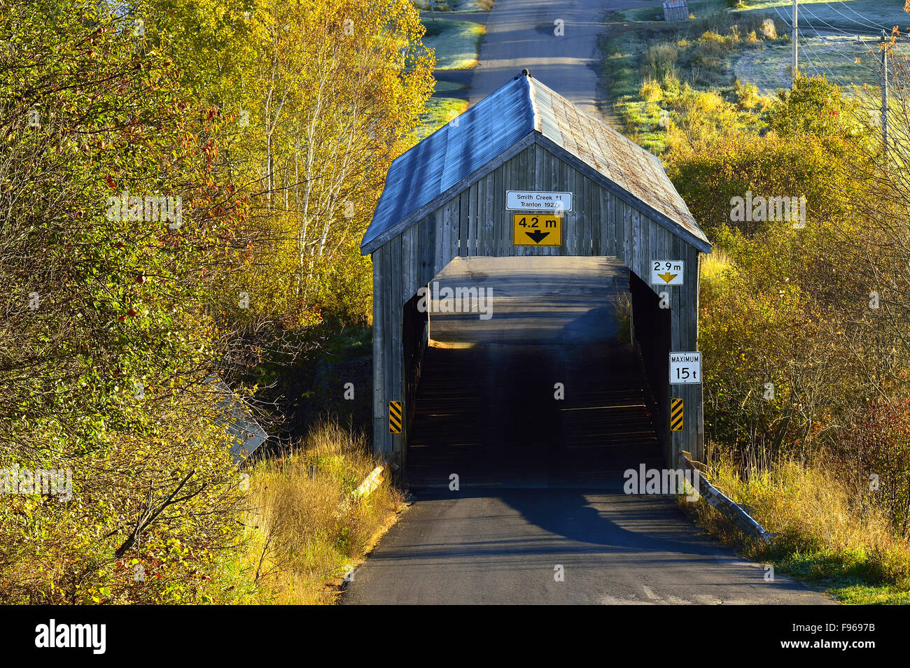 A fall landscape image showing a one lane wooden covered bridge ...