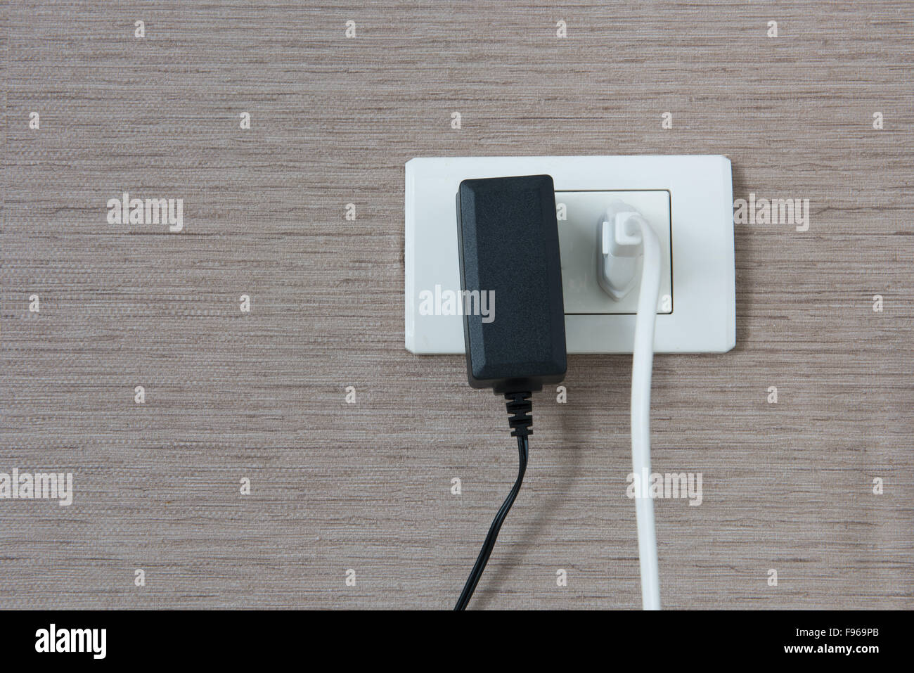 White and black cable plugged in a white electric outlet mounted on ...