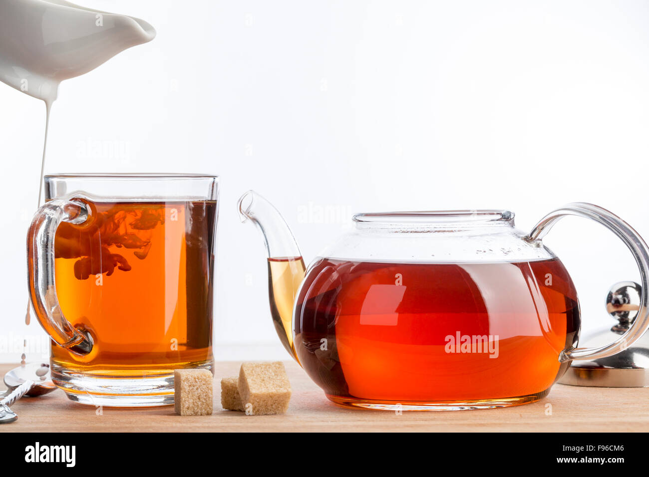 Spilled milk for cup of tea. Transparent cup and teapot on a white ...