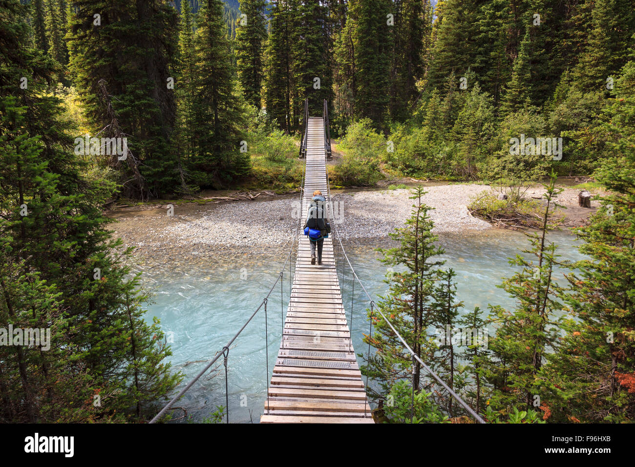 A back packer crosses a suspension bridge over a river in Kootenay ...