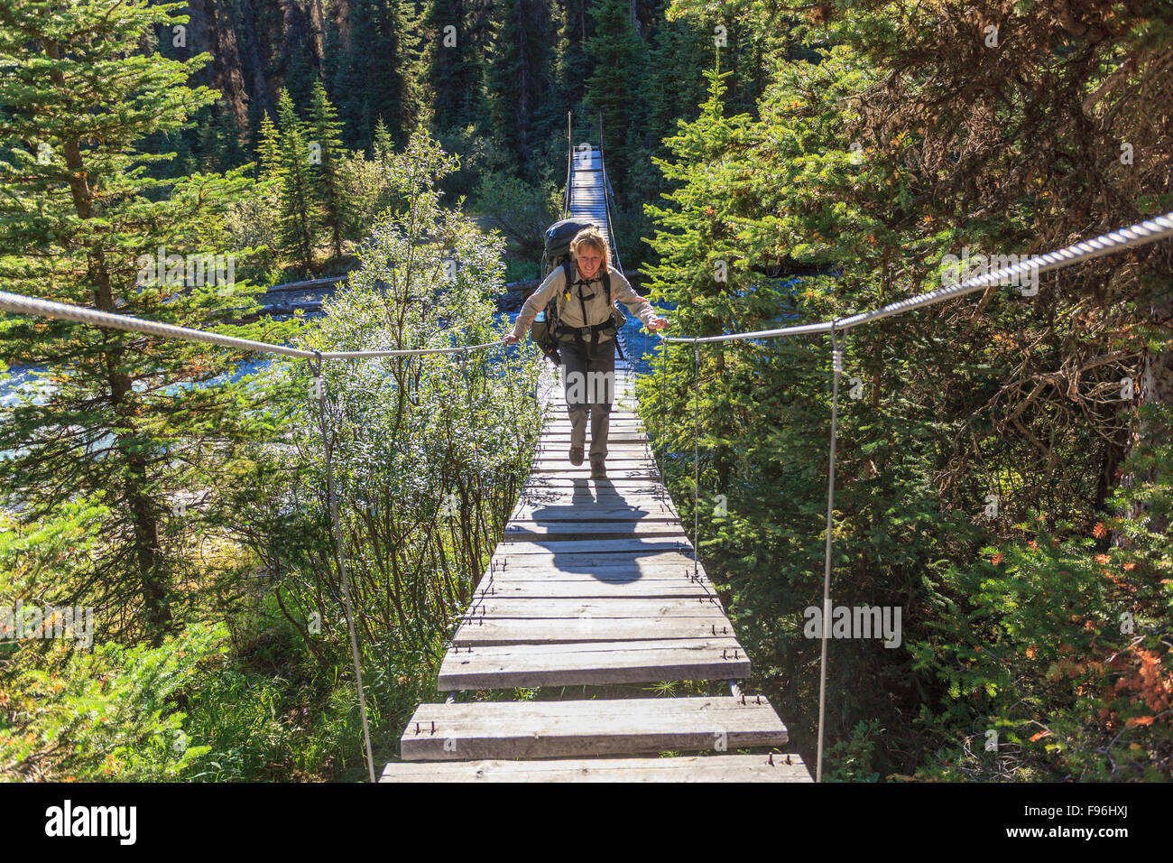 A back packer crosses a suspension bridge over a river in Kootenay ...