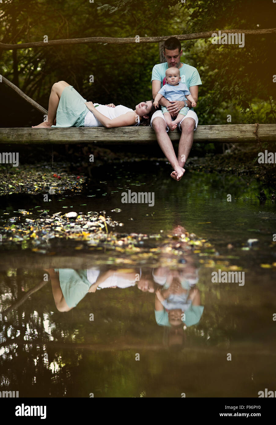 Happy family with little baby boy is sitting on the bridge over the ...