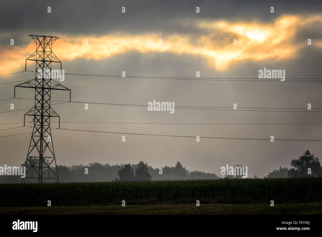 Electric power lines and tower and split in clouds with rising sun ...