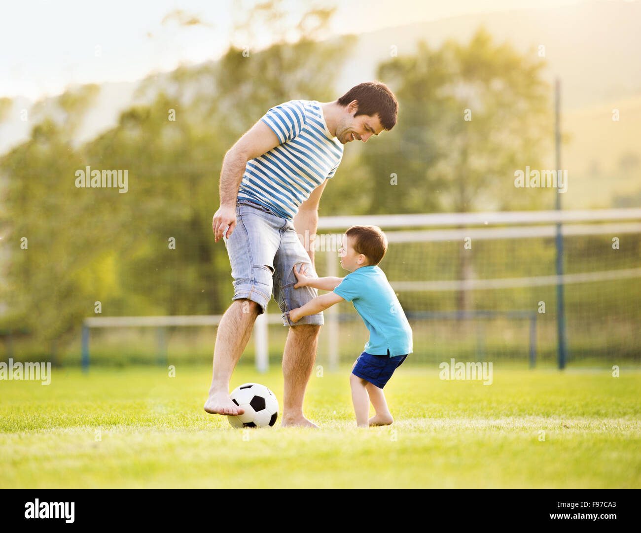 Young father with his little son playing football on football pitch ...