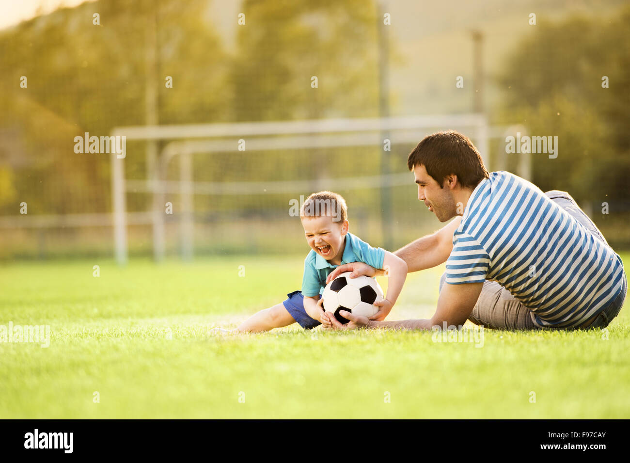 Young father with his little son playing football on football pitch ...