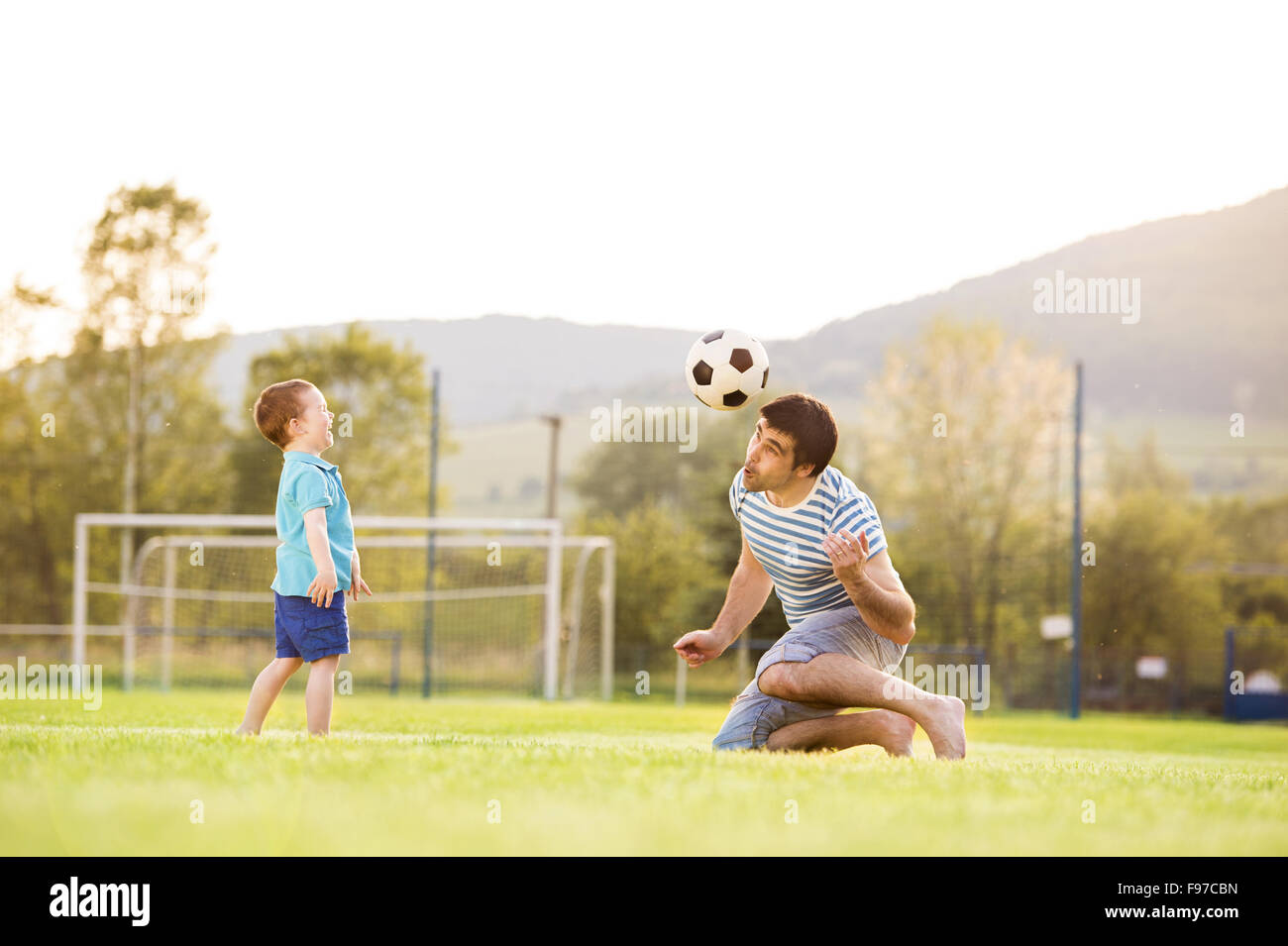 Young father with his little son playing football on football pitch ...