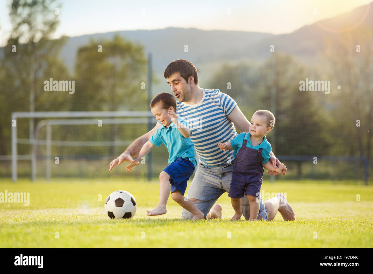 Young father with his little sons playing football on football pitch ...