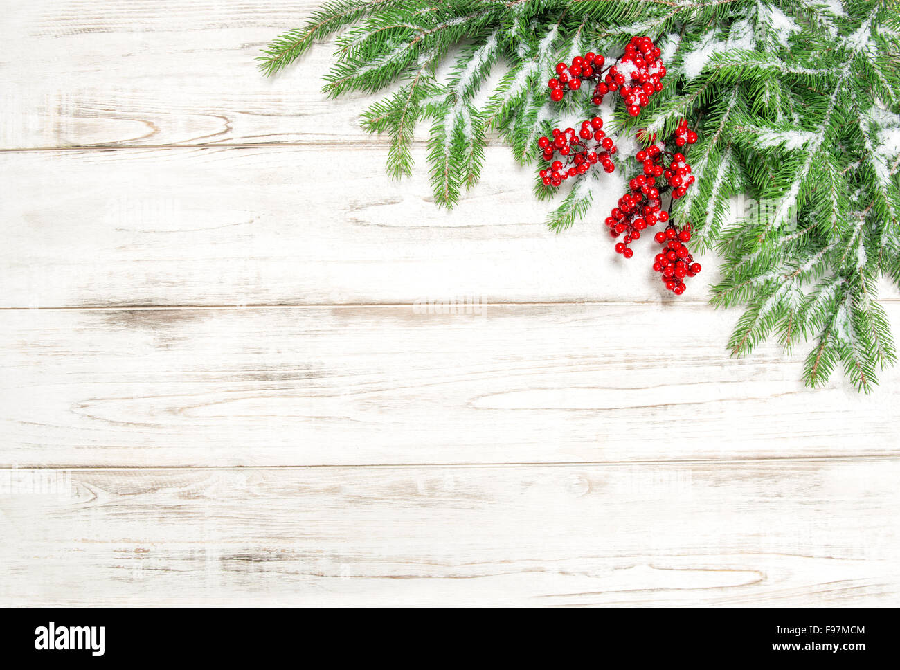Christmas tree sprigs with red berries and snow on wooden background ...