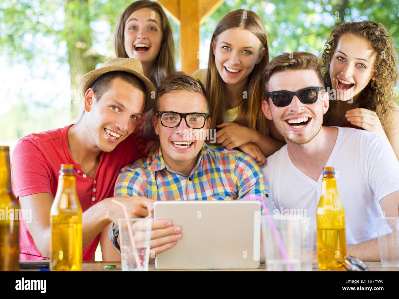 Group of happy friends drinking and having fun with tablet in pub ...