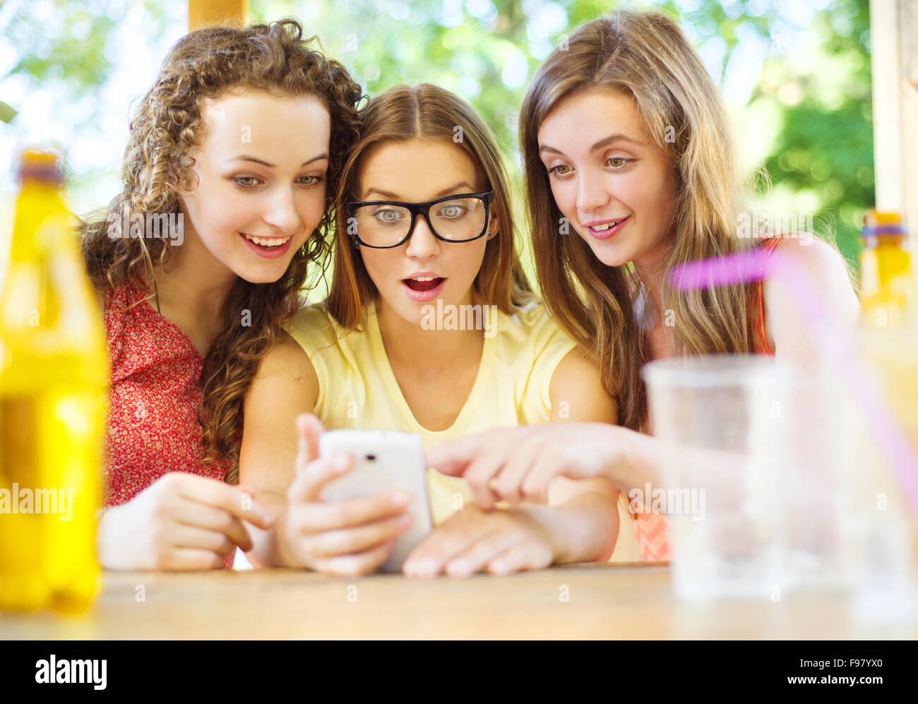 Three beautiful girls drinking and having fun with smartphone in pub ...