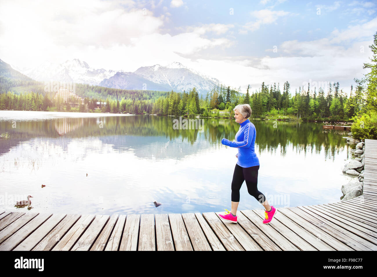 Senior woman jogging round the tarn in beautiful mountains, hills and ...