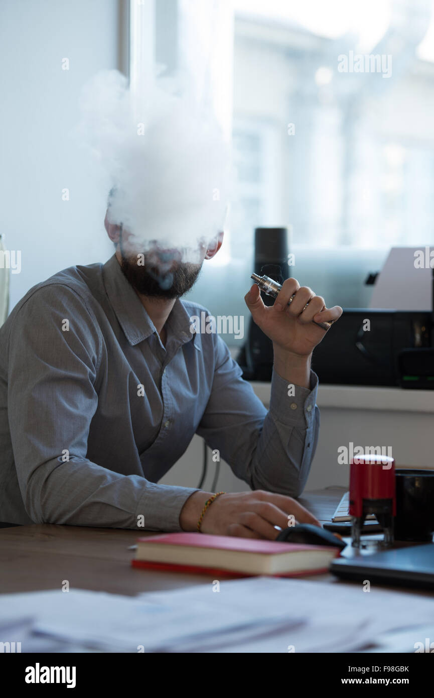 Handsome businessman working with computer in office and vaping ...