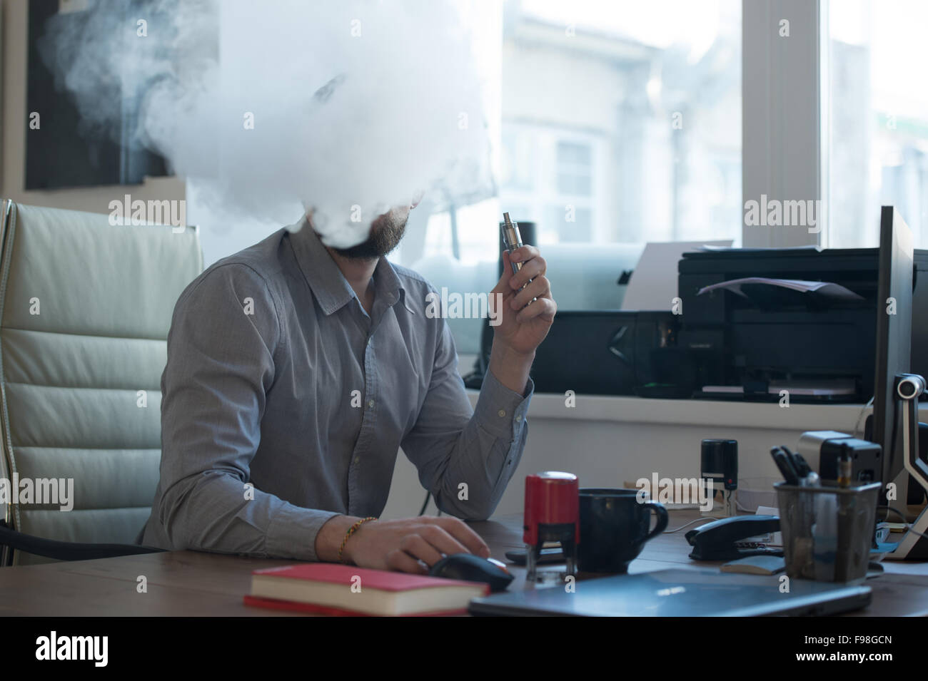 Handsome businessman working with computer in office and vaping ...