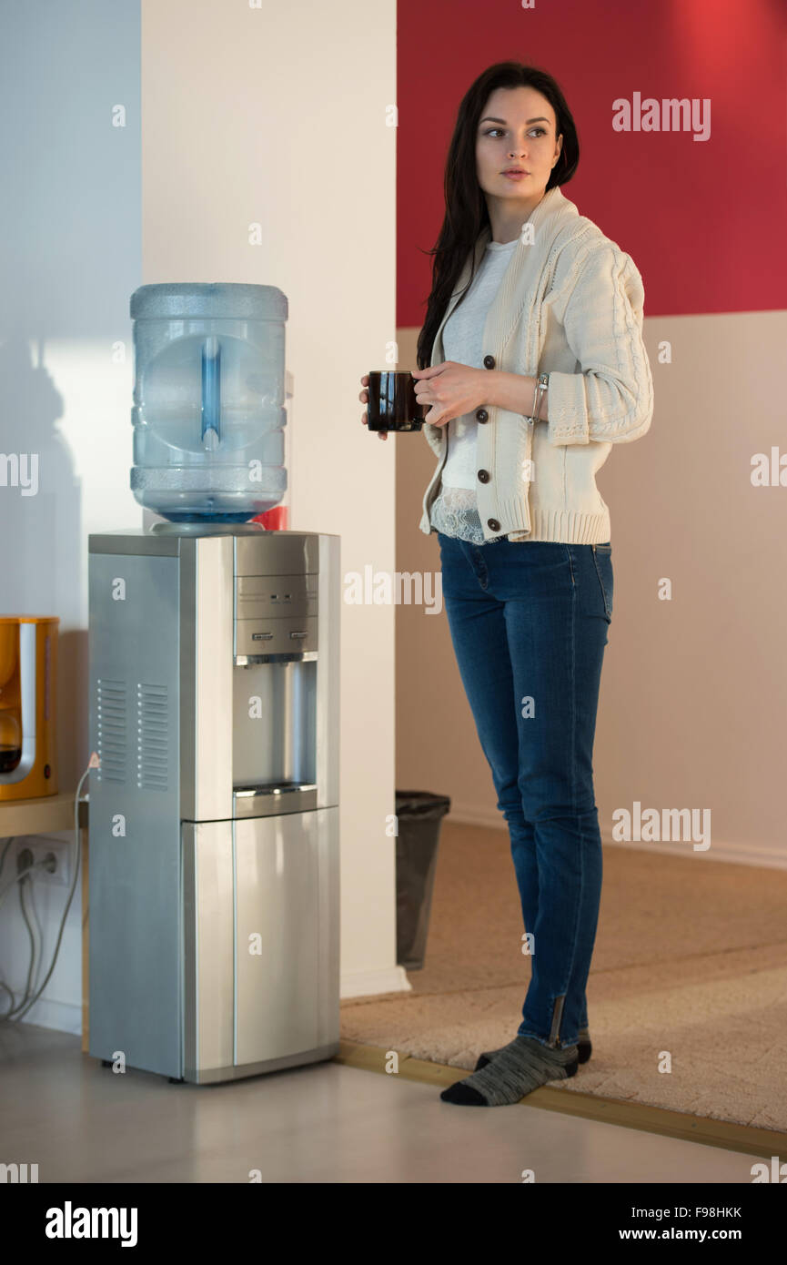 Young woman using water dispenser at office Stock Photo - Alamy