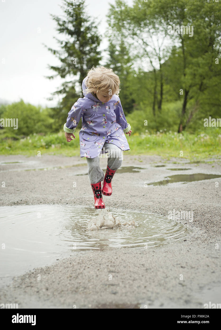 Little girl jumping in a water puddle in green park Stock Photo - Alamy