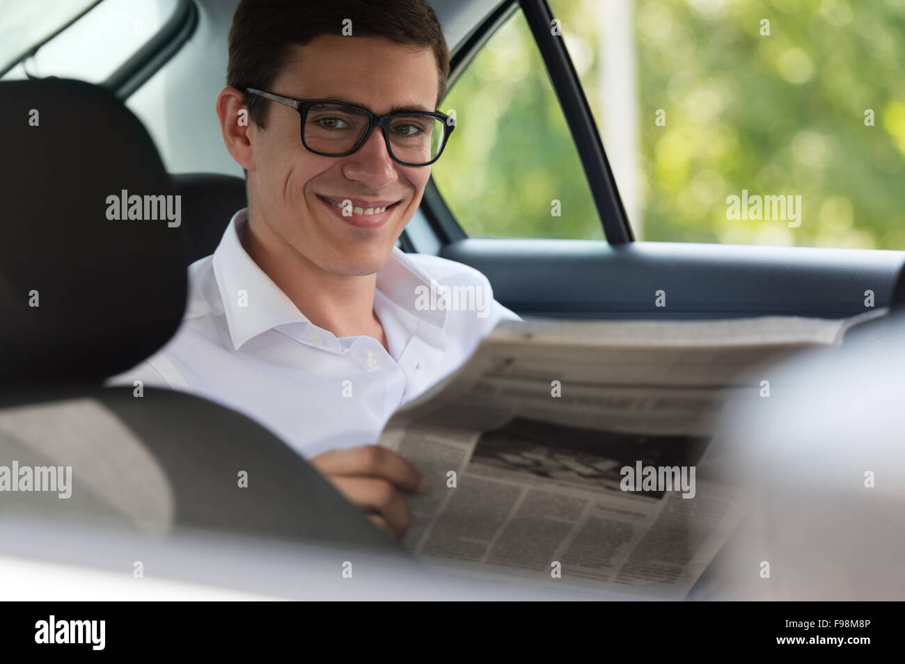 Happy young man reading newspaper in car, smiling Stock Photo - Alamy