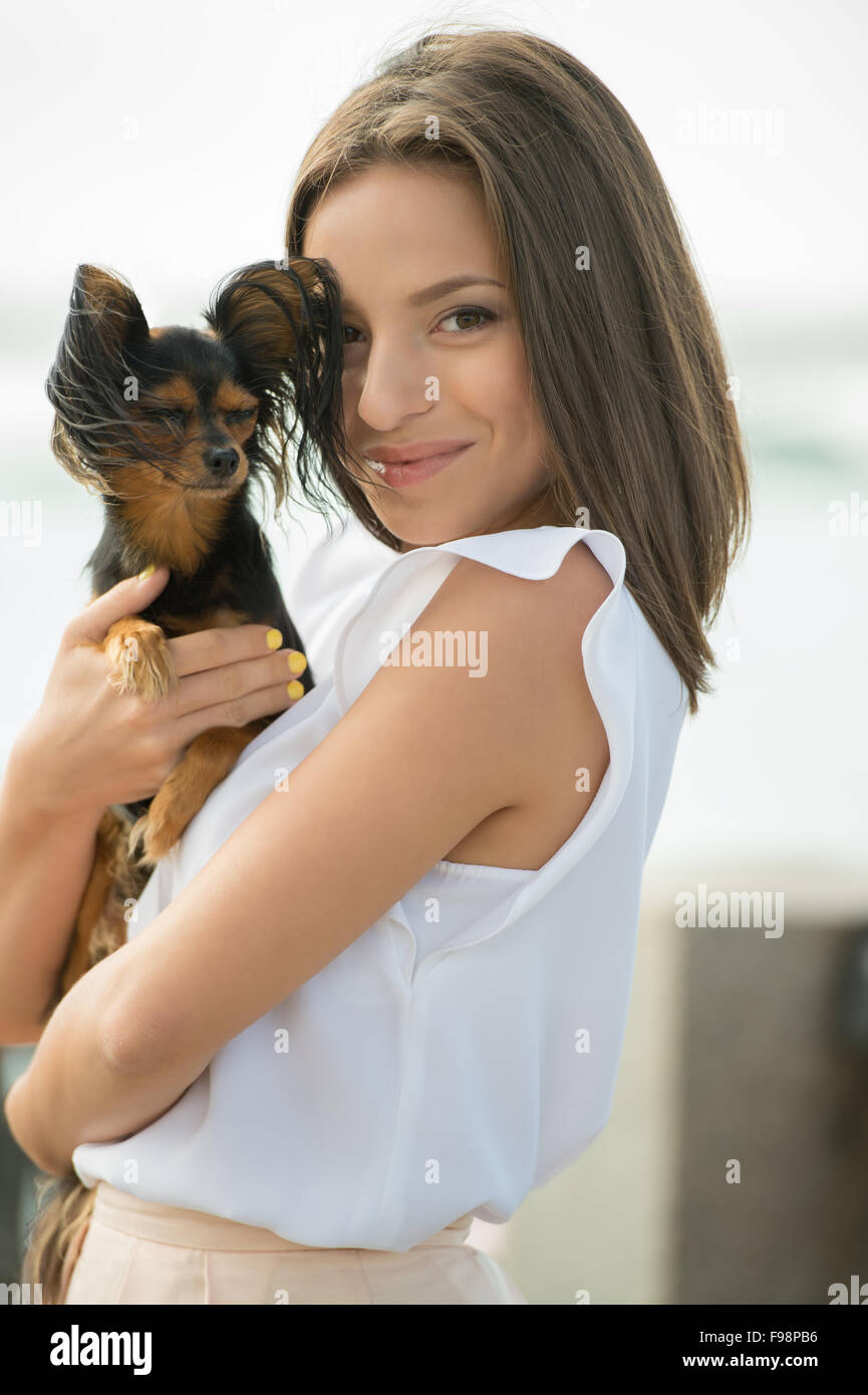 Beautiful young woman wearing elegant dress holding small dog while ...