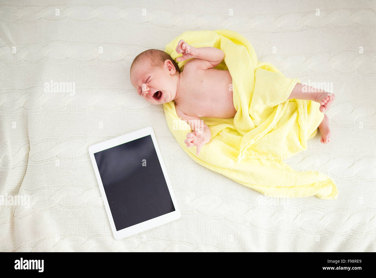 Crying newborn baby girl lying on bed next to digital tablet Stock ...