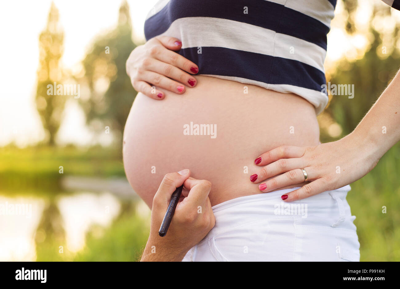 Man is writing a name on pregnant woman's belly in nature Stock Photo ...