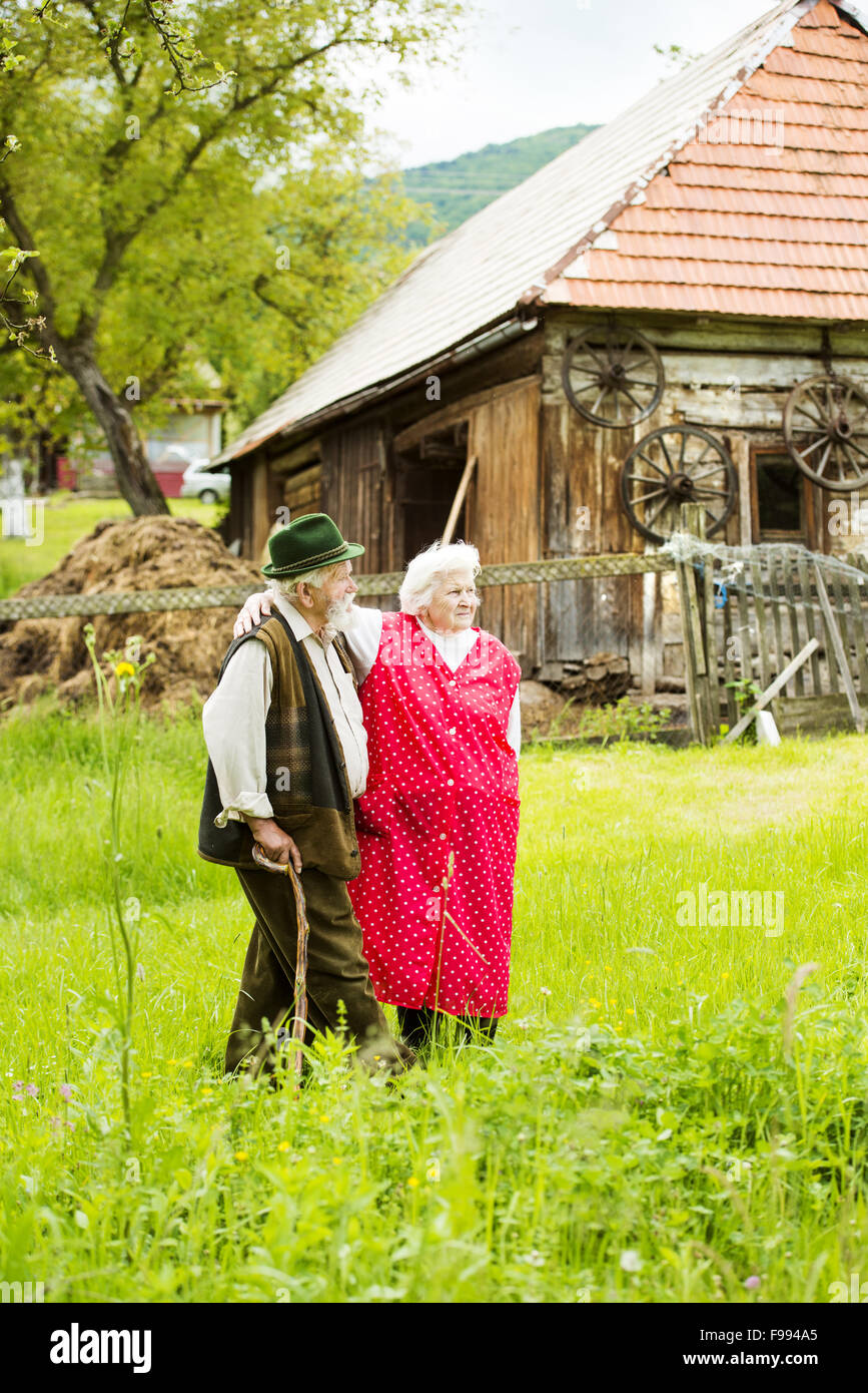 Outdoor portrait of old farmers couple standing by their farmhouse ...