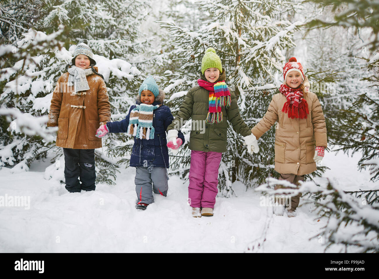 Cheerful kids in winter-wear looking at camera on background of fir ...