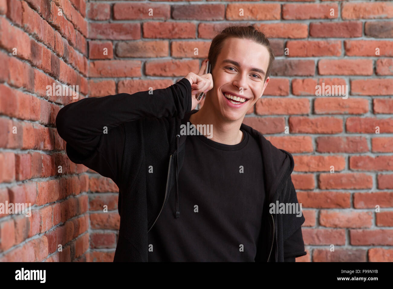 Portrait of a cheerful man talking on the phone over brick wall ...