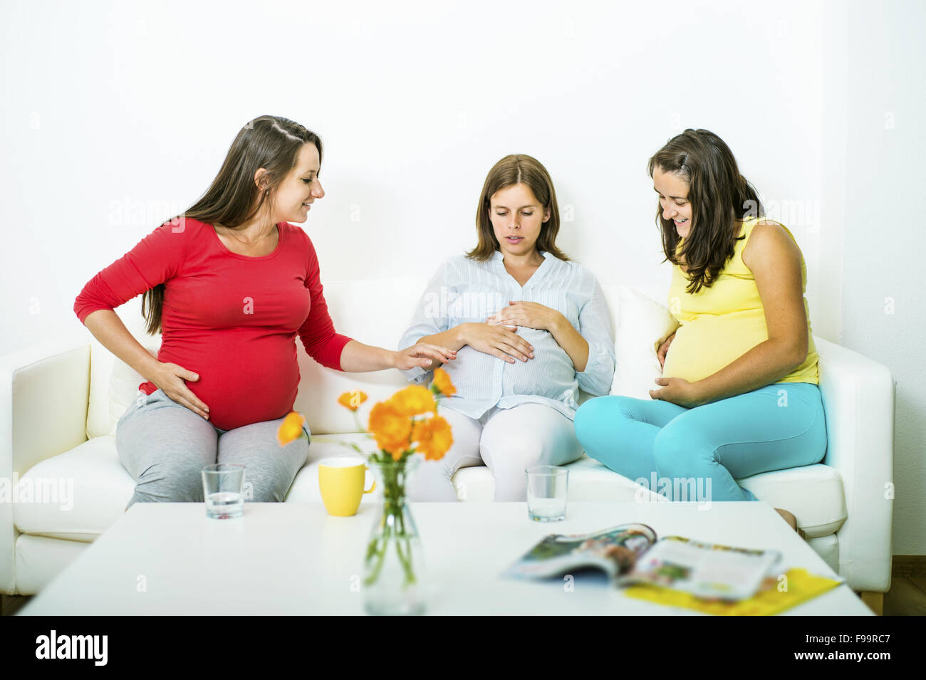 Three pregnant women sitting on sofa and chatting Stock Photo - Alamy