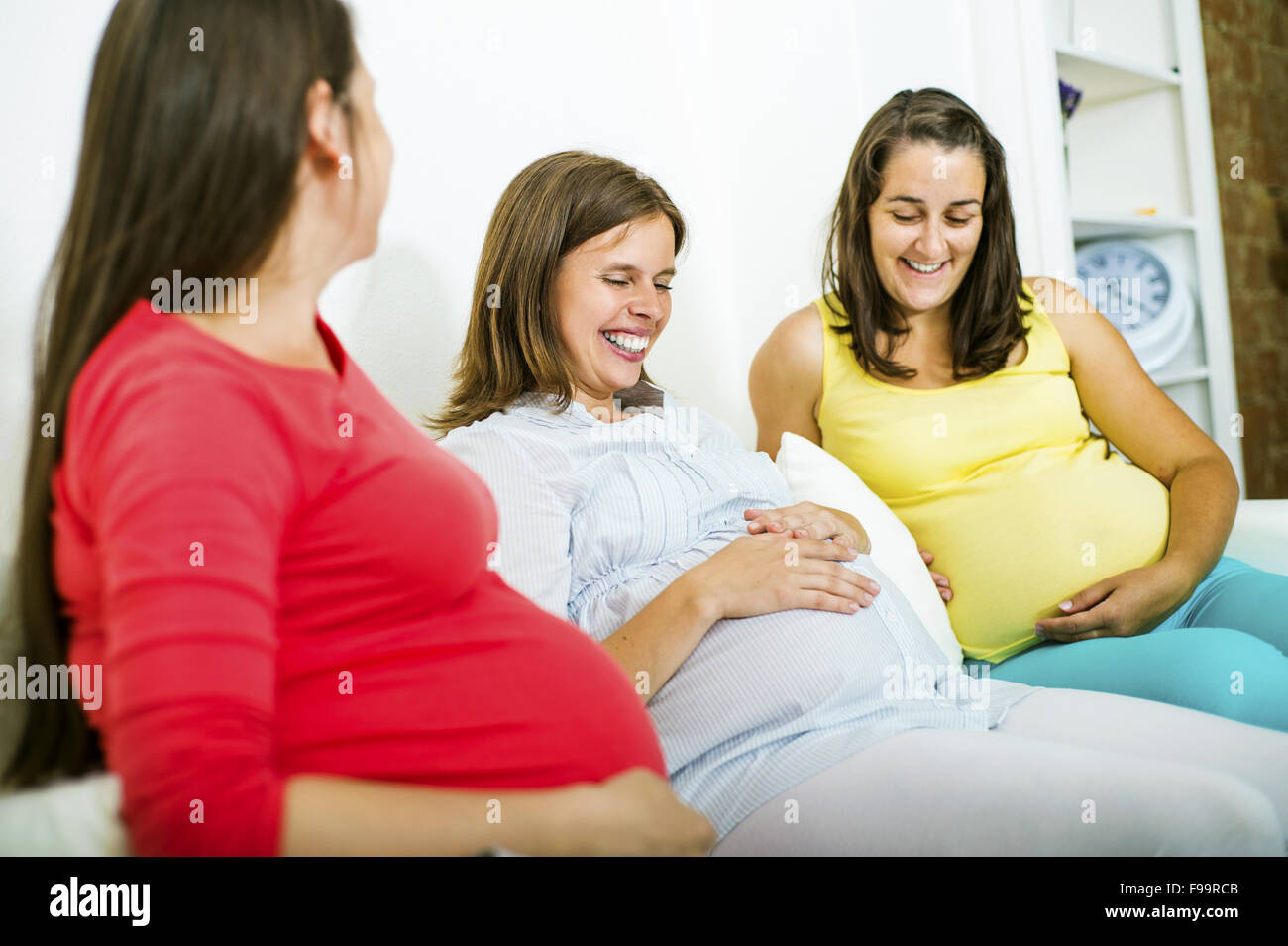 Three pregnant women sitting on sofa and chatting Stock Photo - Alamy