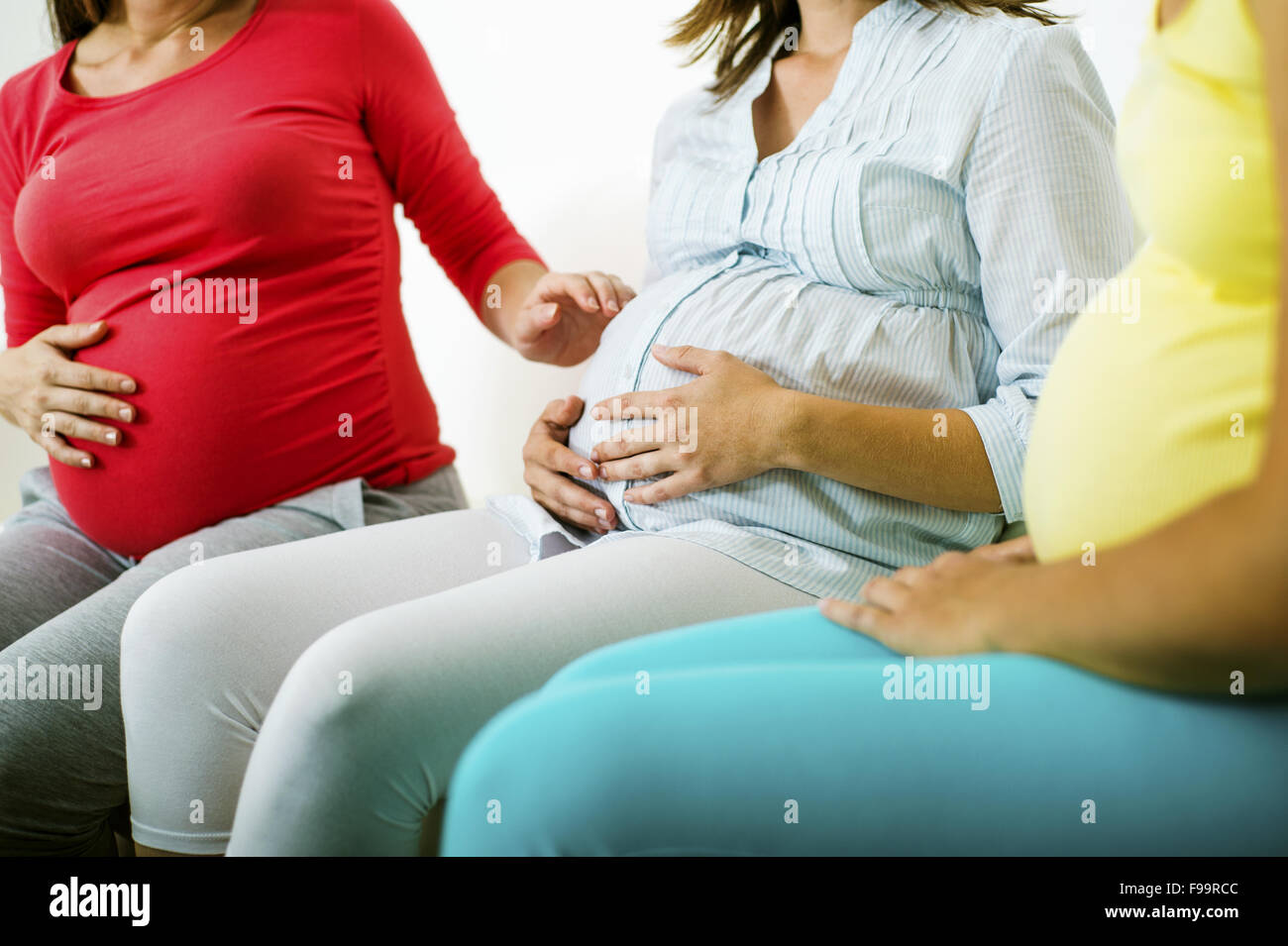Three pregnant women sitting on sofa and chatting Stock Photo - Alamy