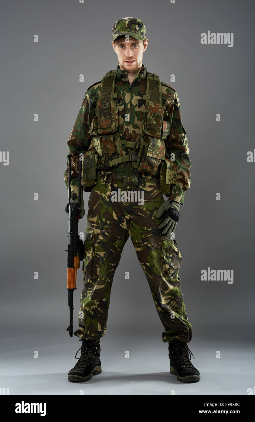 Studio portrait of an young soldier in uniform with machine gun, over ...