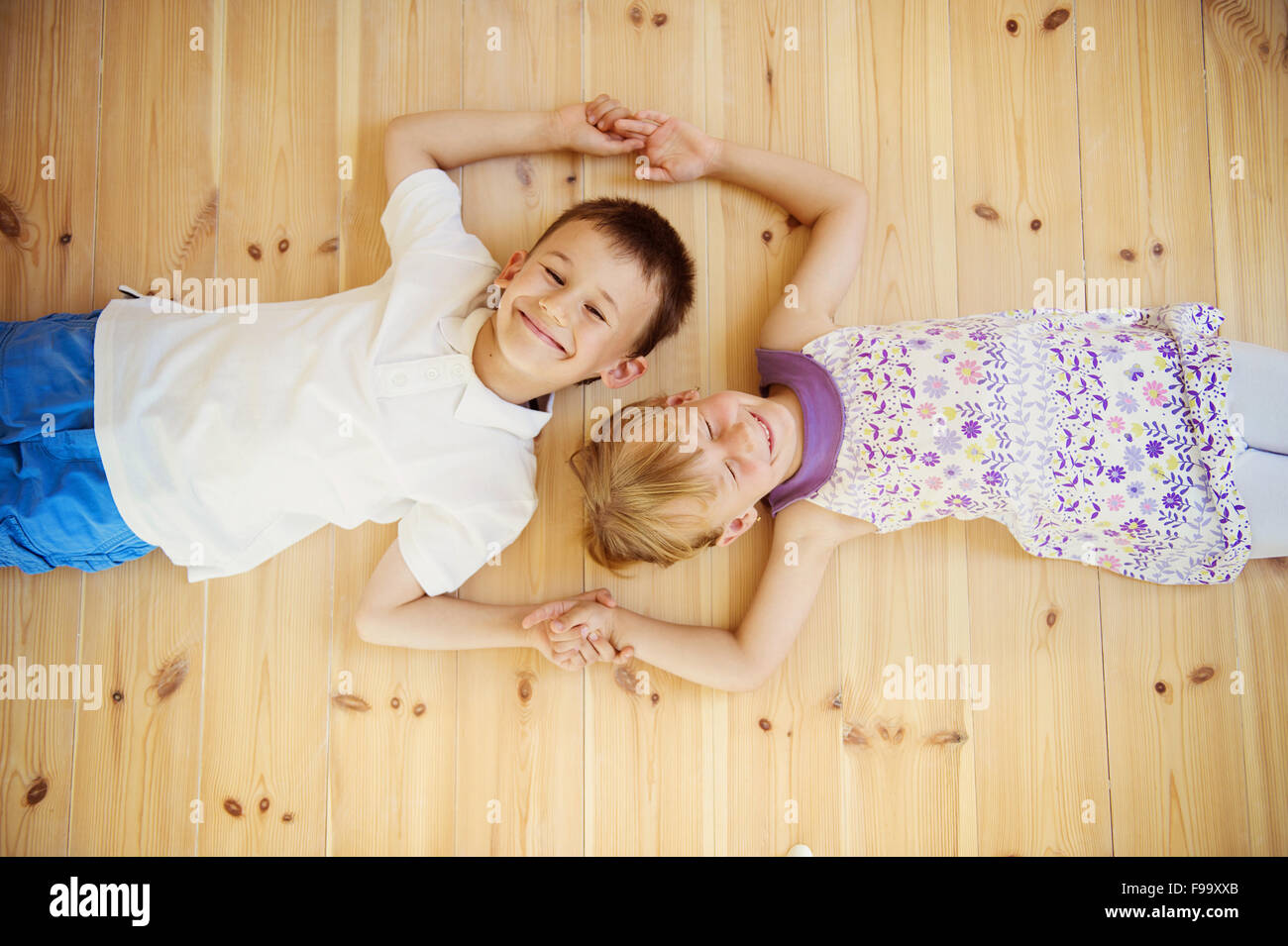 Two kids lying down on the wooden floor in house Stock Photo - Alamy