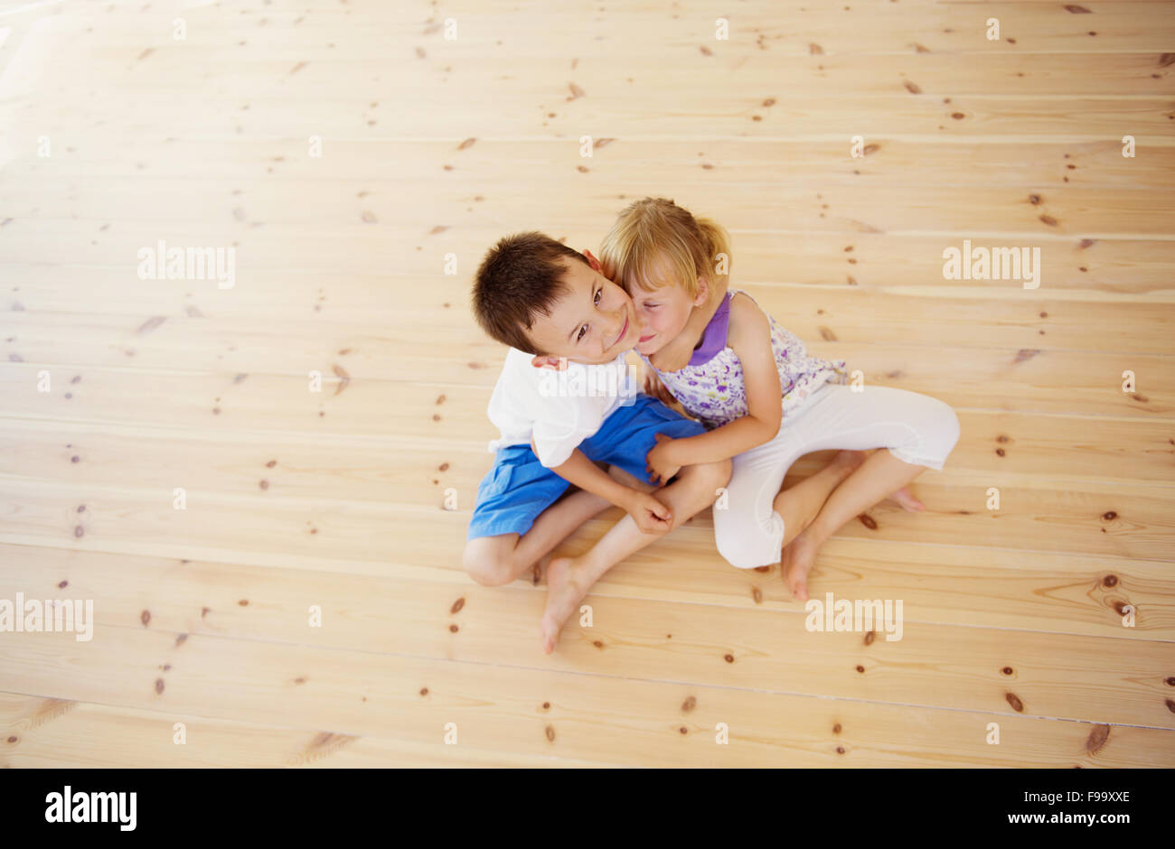 Two kids lying down on the wooden floor in house Stock Photo - Alamy