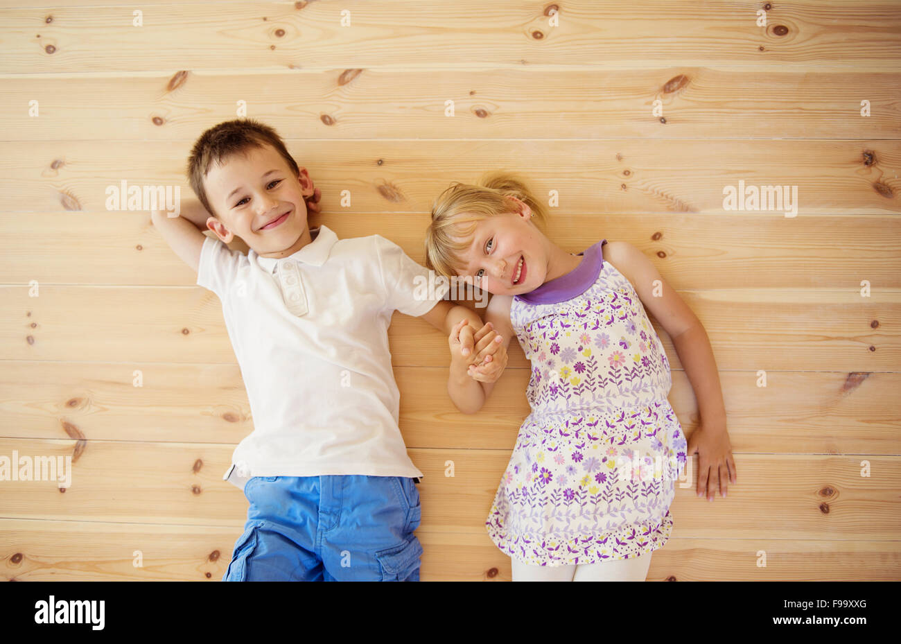 Two kids lying down on the wooden floor in house Stock Photo - Alamy