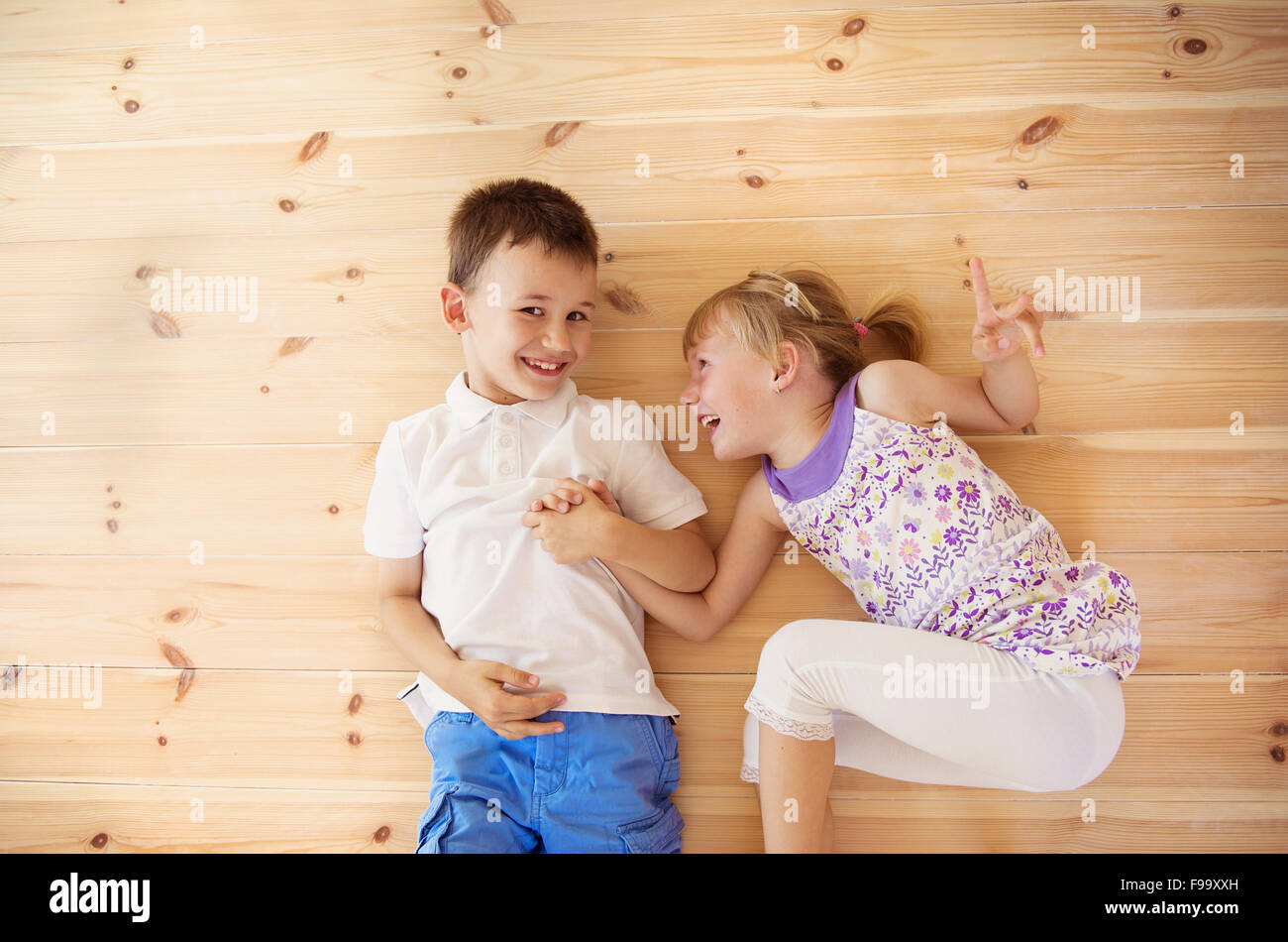 Two kids lying down on the wooden floor in house Stock Photo - Alamy