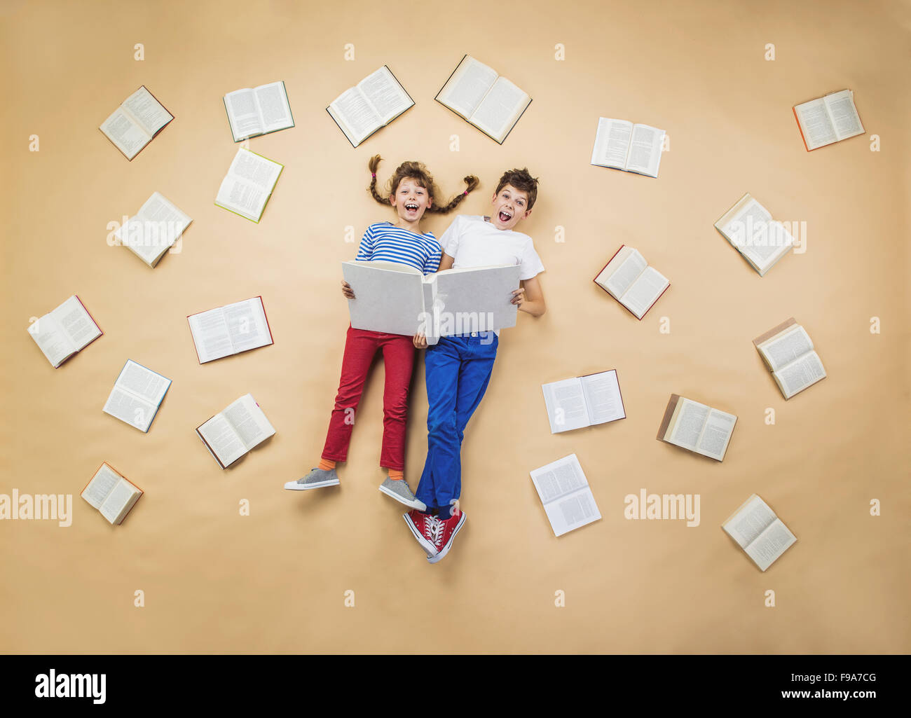 Happy children are reading book on the floor with group of books around ...