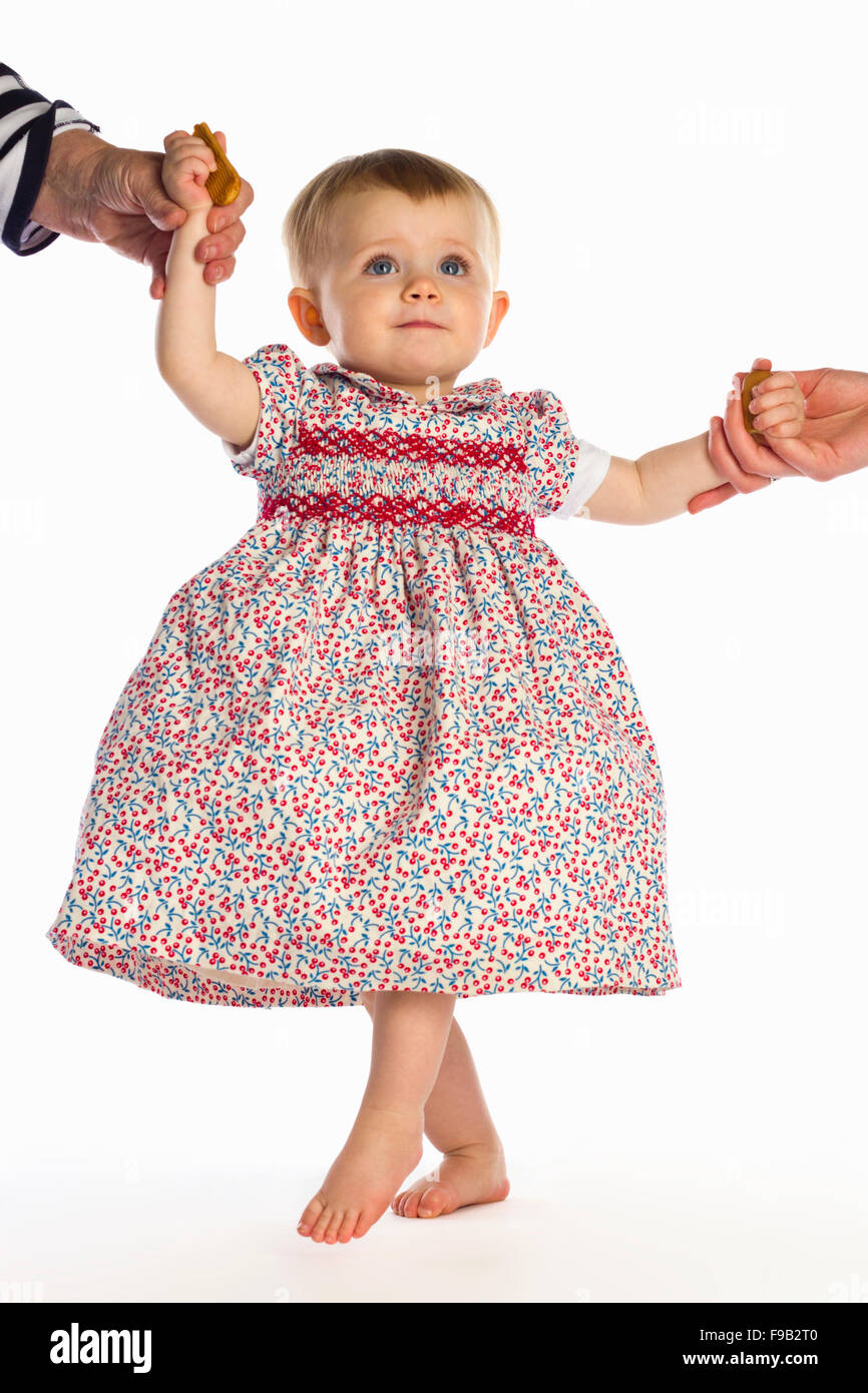 Studio portrait of cute baby girl standing and supported by mum and ...